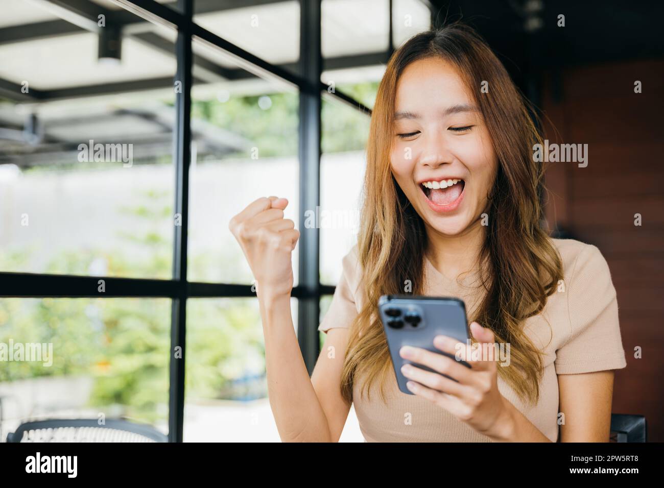 Asian young woman celebrating work success near windows in morning with ...