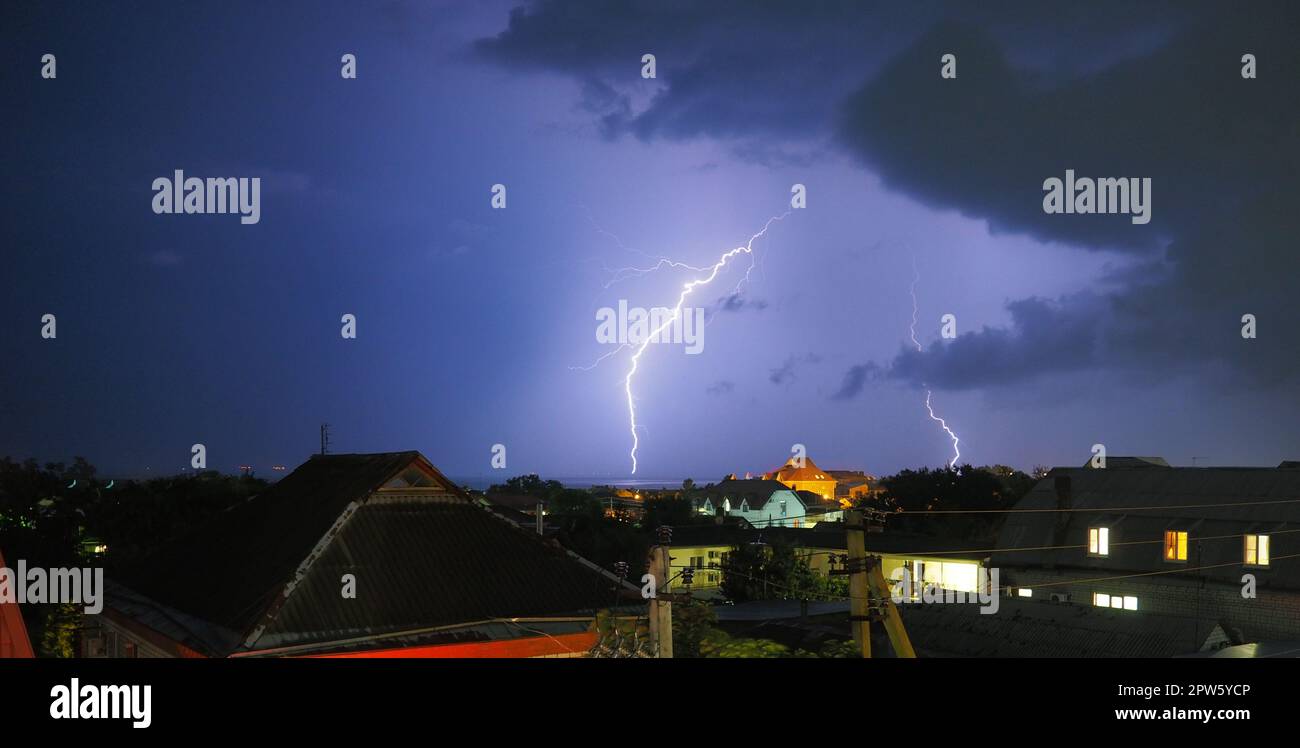 Two lightning bolts against the background of a dark sky with clouds. Thunderstorm over the city ...