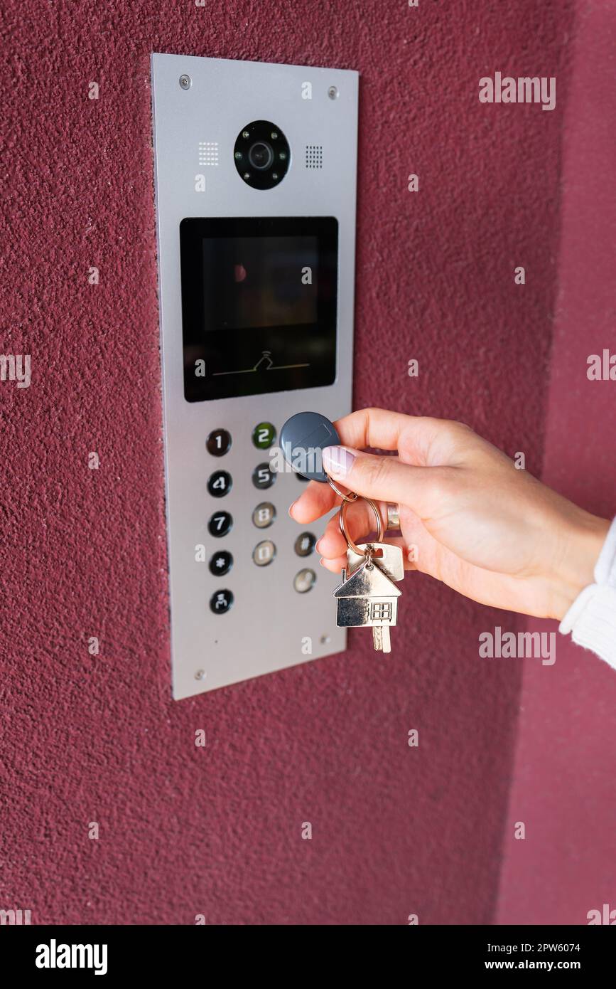 A young woman types the apartment code on the electronic intercom panel ...