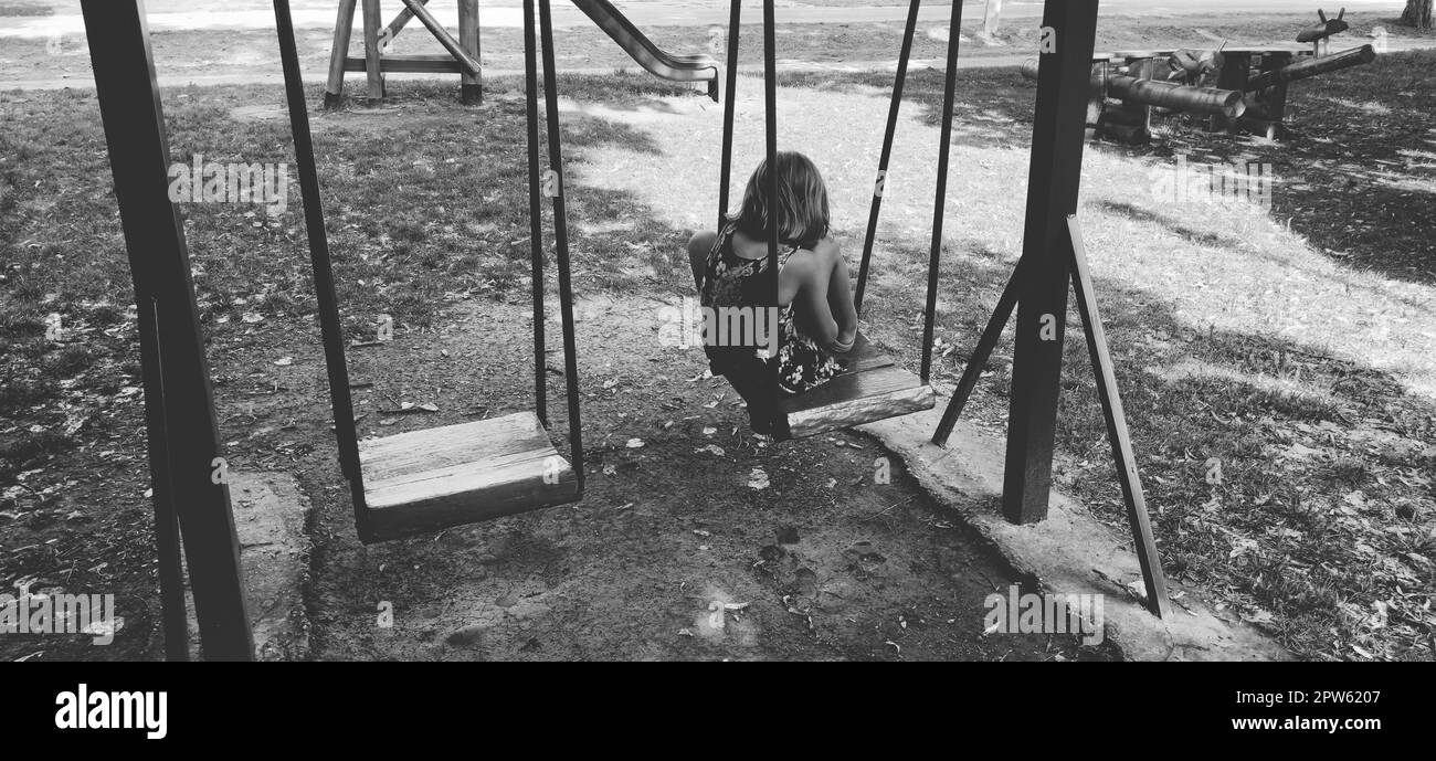 Little girl on the swing. The girl is sad alone on the playground ...