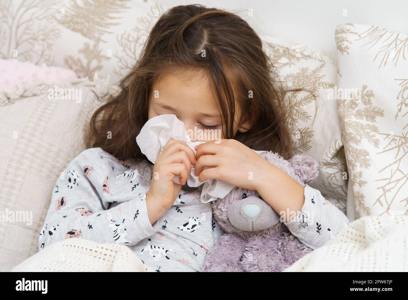Tired, sleepy little brunette girl sneezing snot with tissues ...