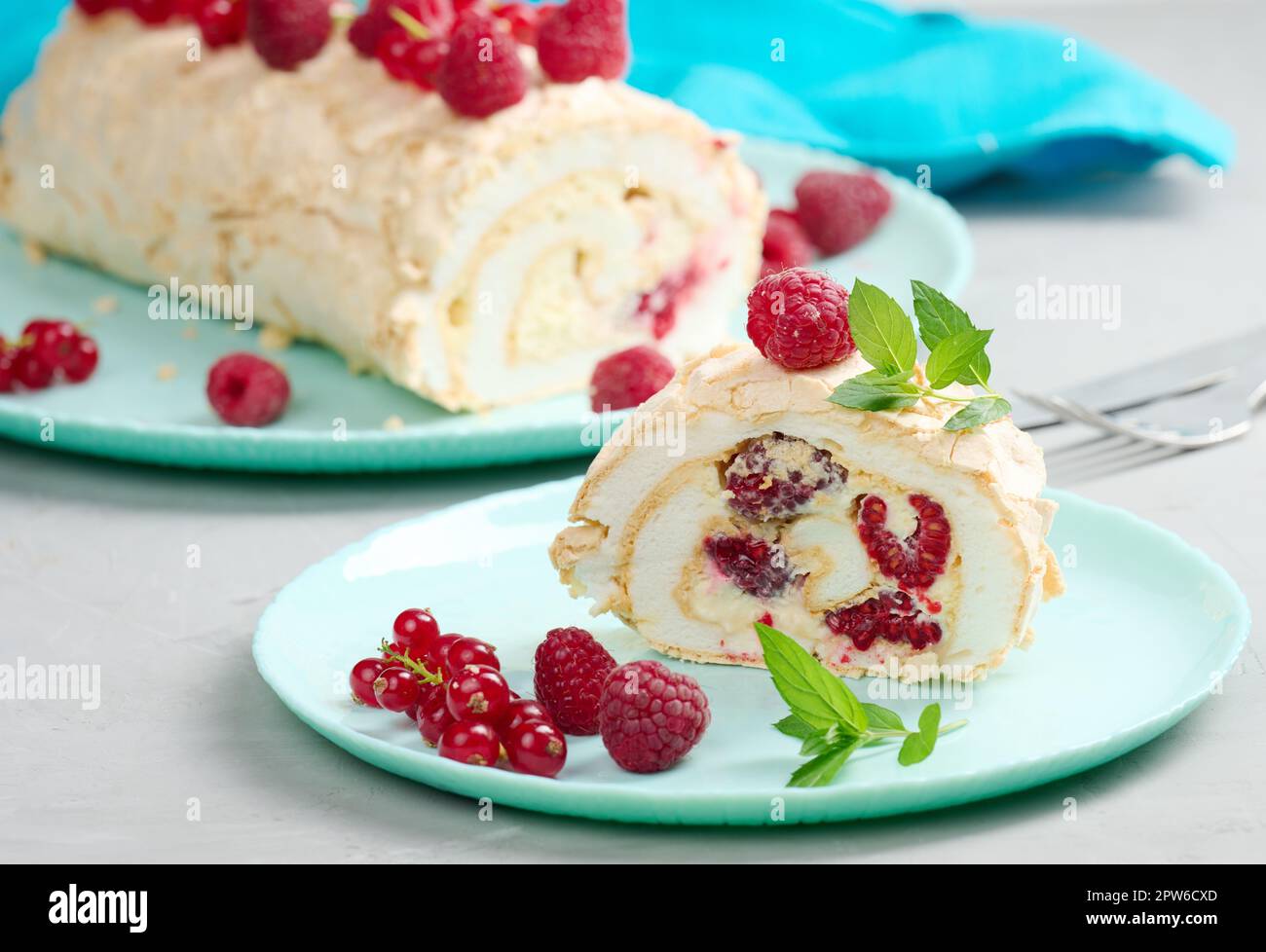 Baked meringue roll with red berries on a round plate, white background ...