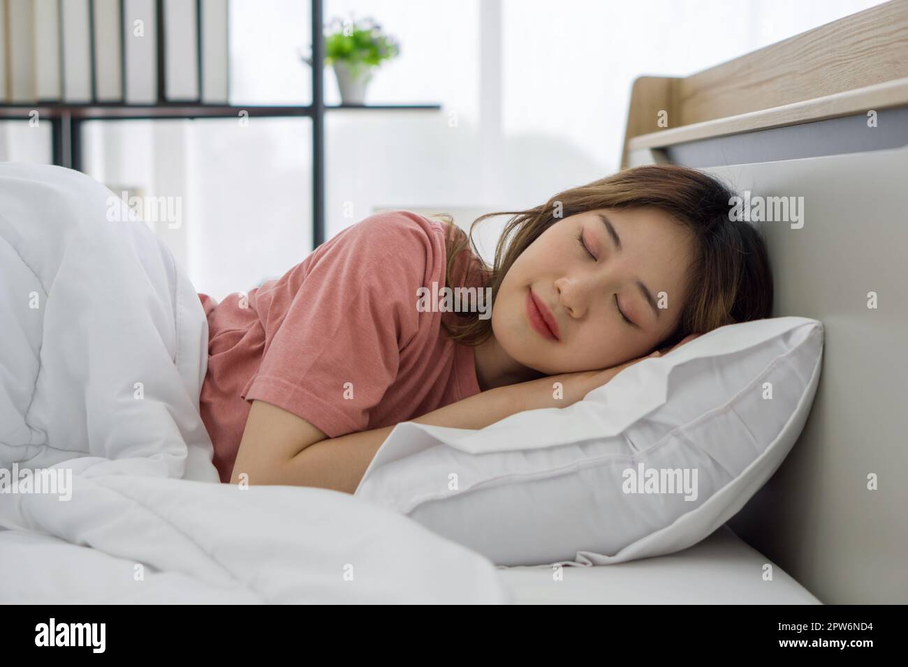 Young Asian woman in pink pajamas sleeping in bed leaning on pillows ...