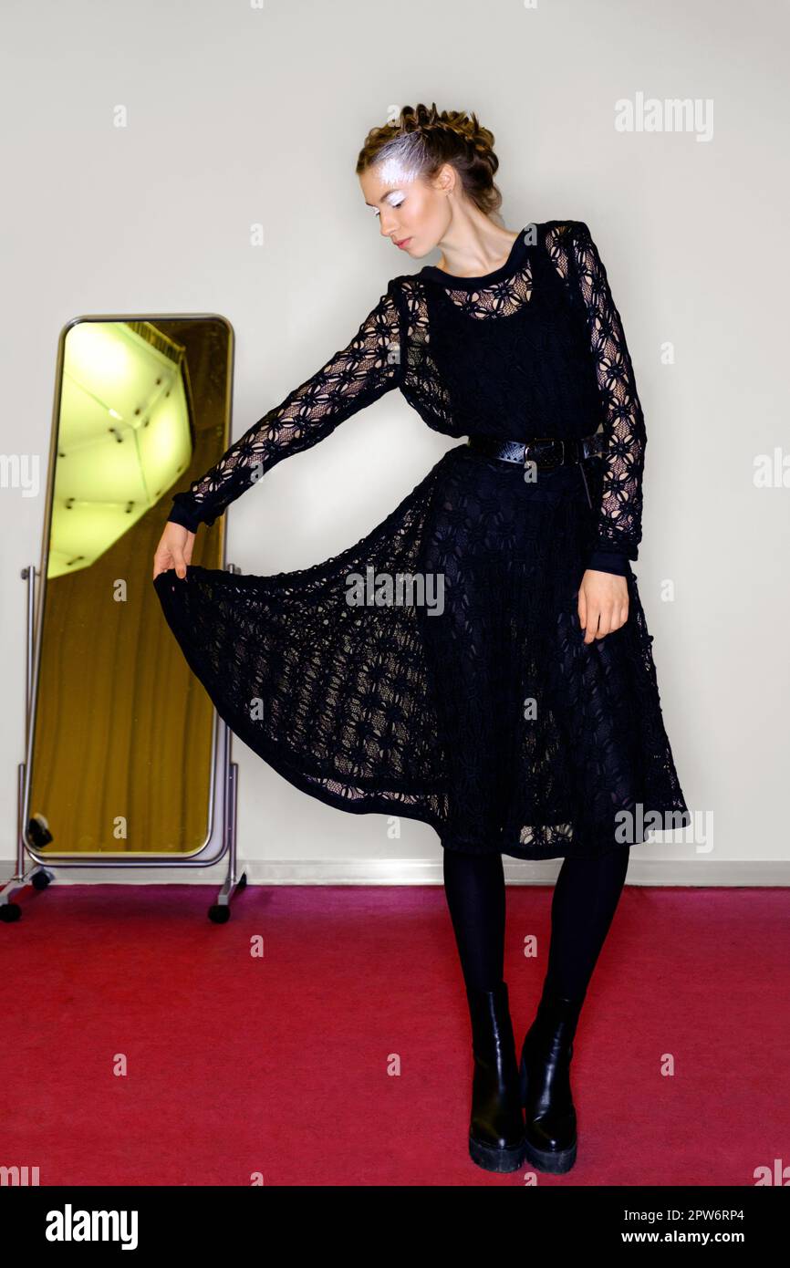 Young woman lifting hem of black knitted dress, standing near the ...