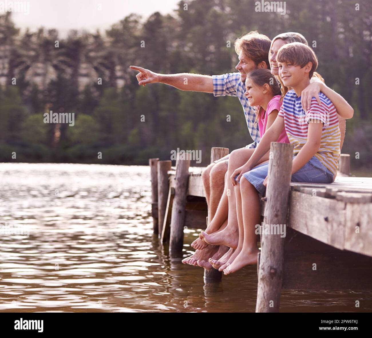 Look down there. A happy family of four sitting on a jetty at the lake Stock Photo - Alamy