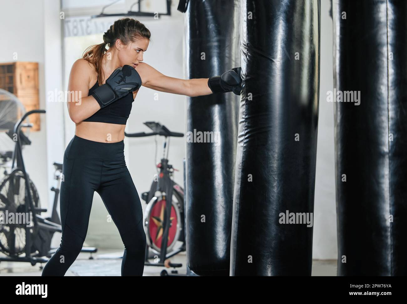 Young, active and strong female boxer punching a boxing bag in the gym ...
