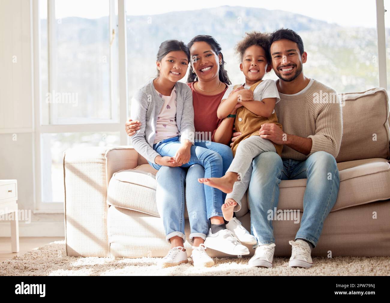 Portrait of two happy parents bonding with their daughters in the lounge, sitting on the sofa ...