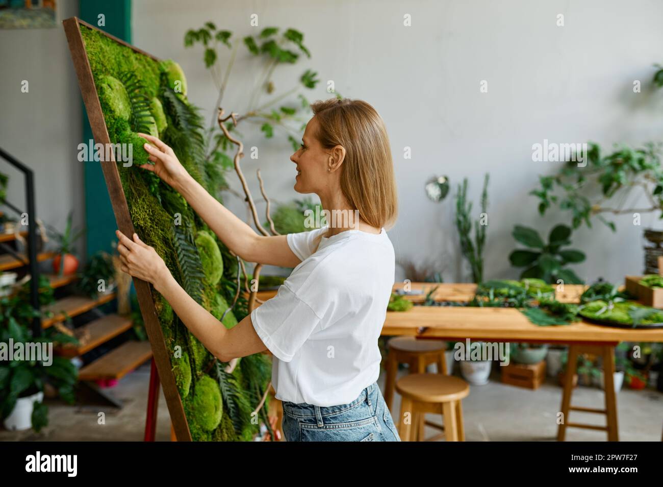 Young happy florist decorator creating plant moss panel. Lovely joyous ...