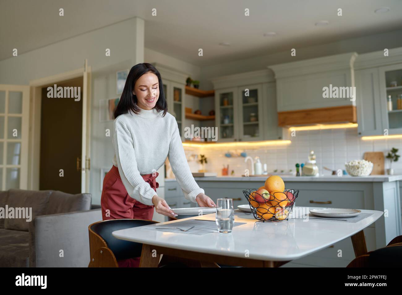 Happy positive smiling woman serving dining table with plates for lunch ...