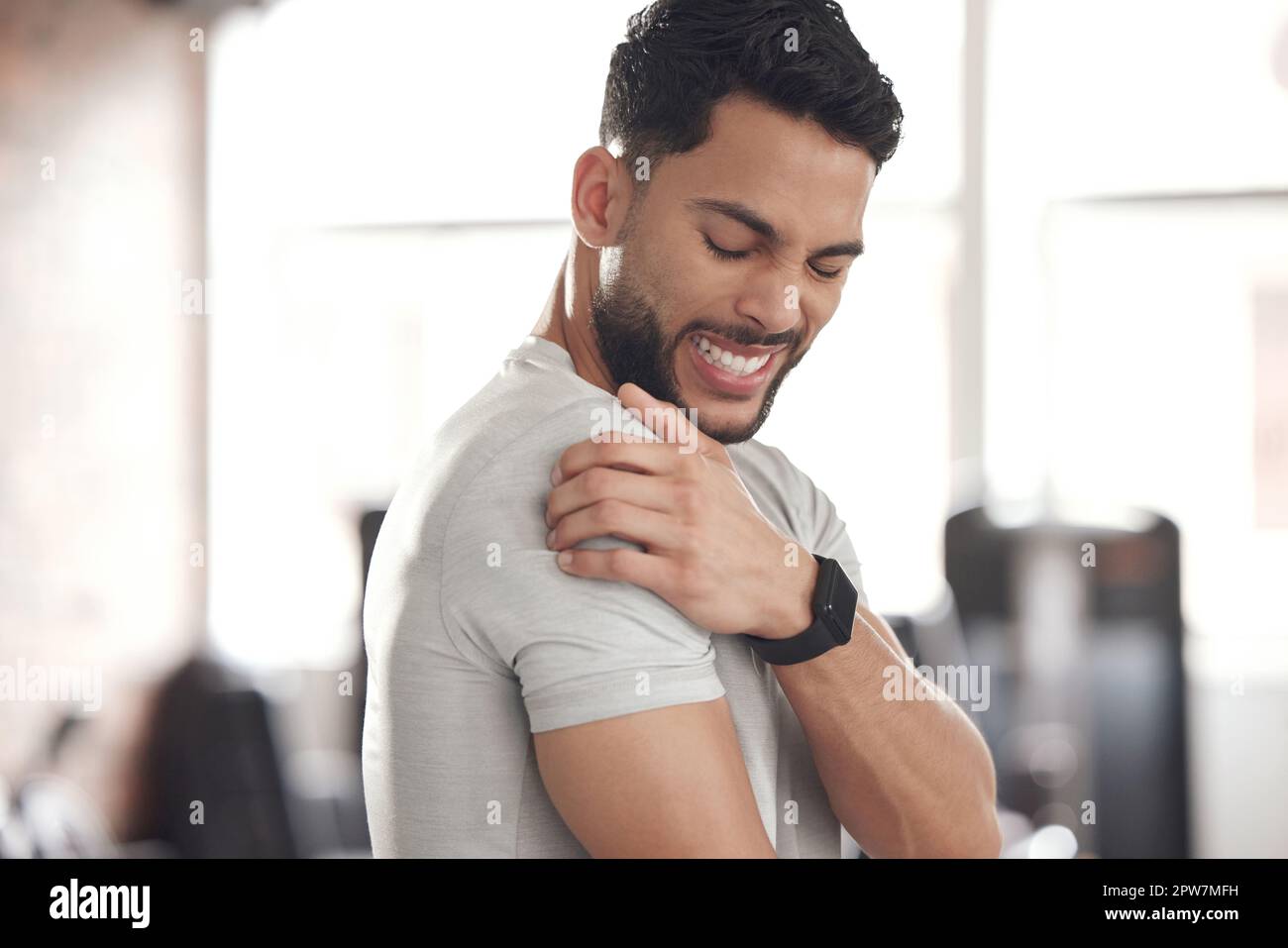 One young hispanic man holding his sore shoulder while exercising in a ...