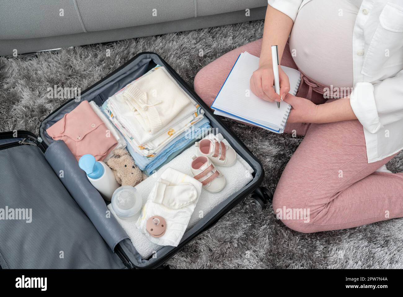 Top view of pregnant woman writing packing list for maternity hospital ...