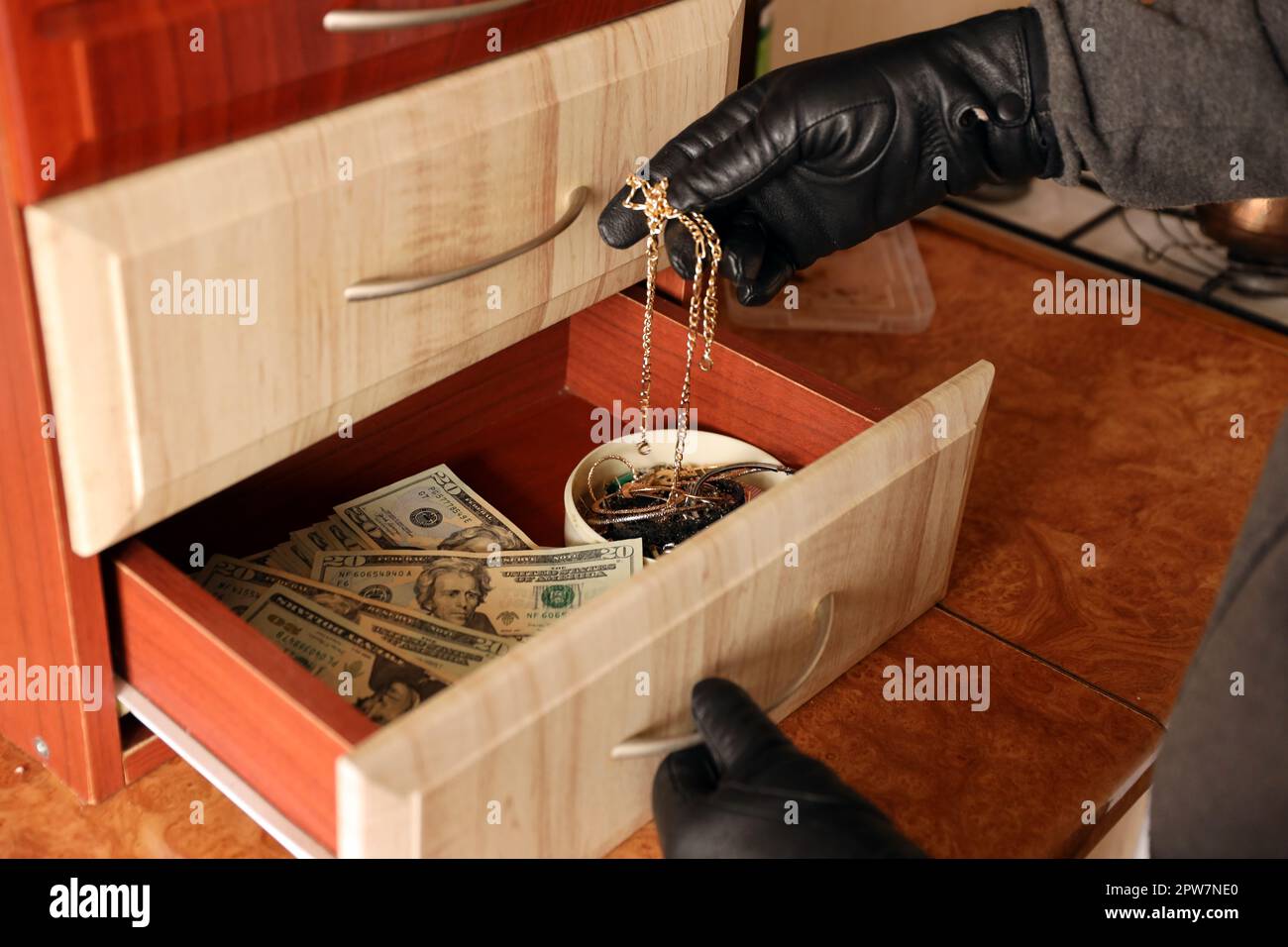 Robber in black outfit and gloves see in opened shelf in kitchen. The ...