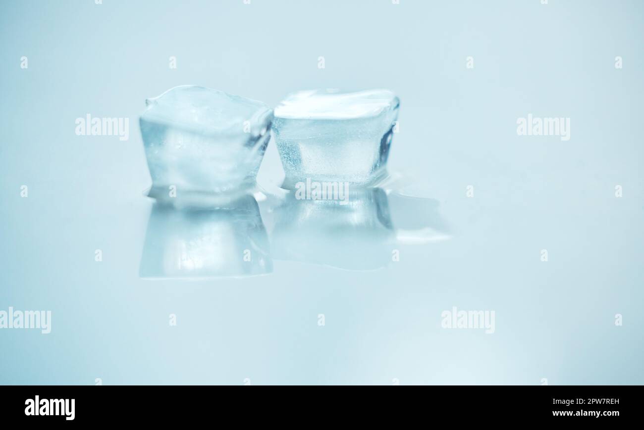Two ice blocks melting side by side against a blue background in studio ...