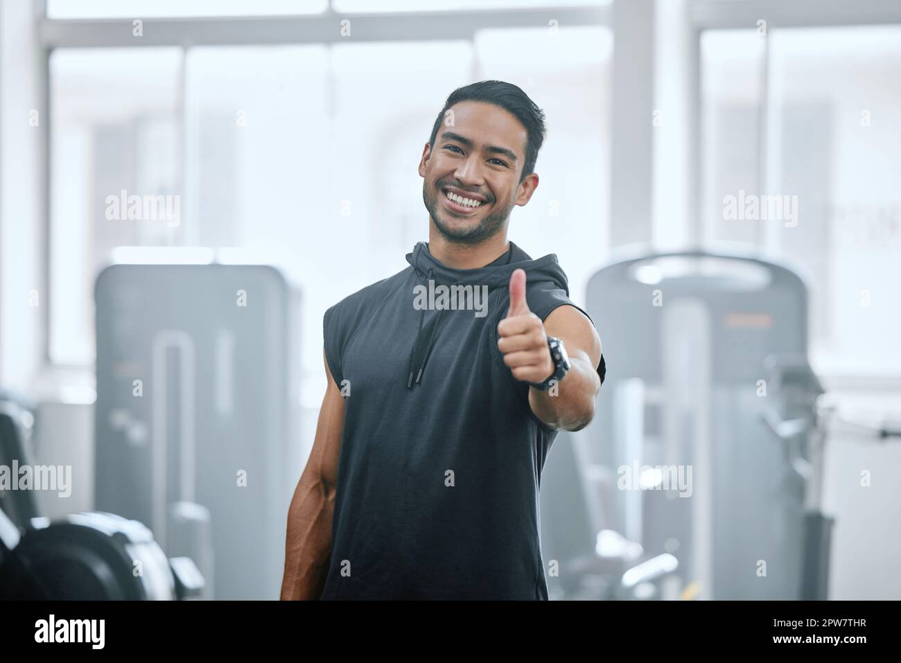 Portrait of smiling trainer alone in gym, showing thumbs up sign and ...