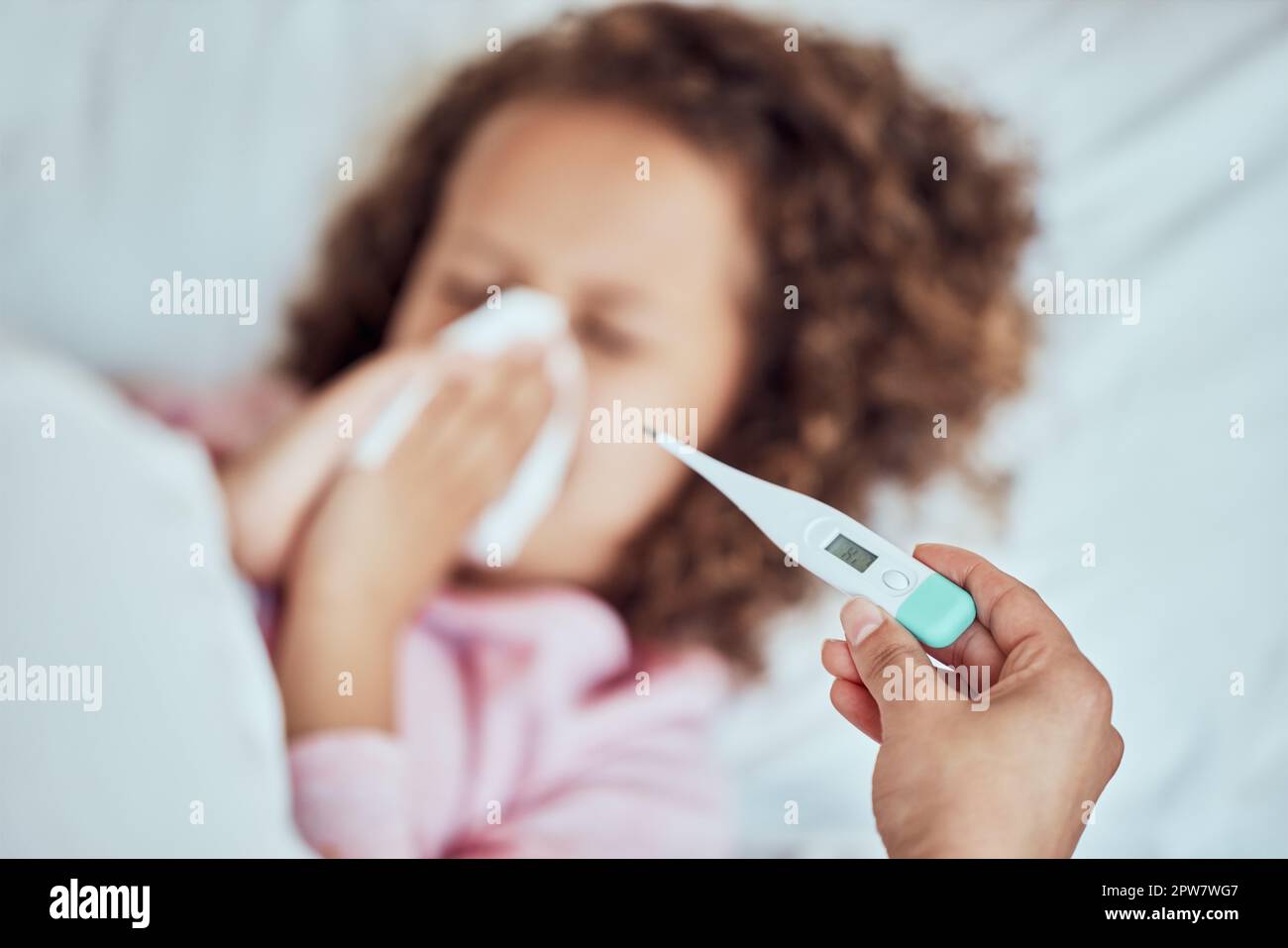 Above mixed race little girl blowing her nose while laying in bed ...