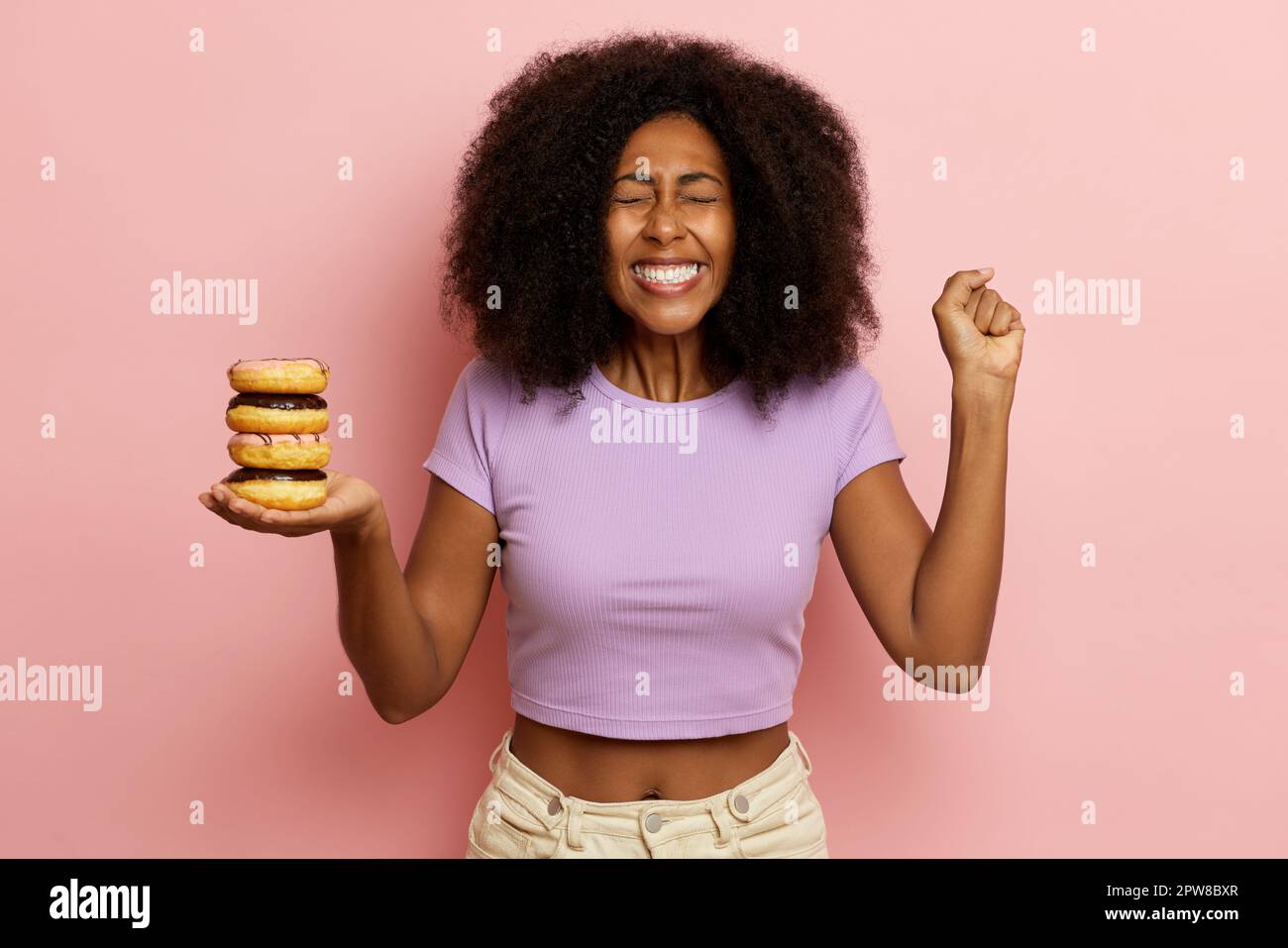 Indoor shot of cheerful curly haired woman with happy expression, keeps ...
