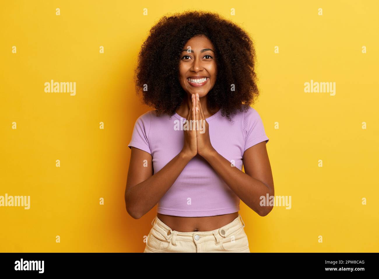 Positive charming curly haired woman holds palms pressed together and ...