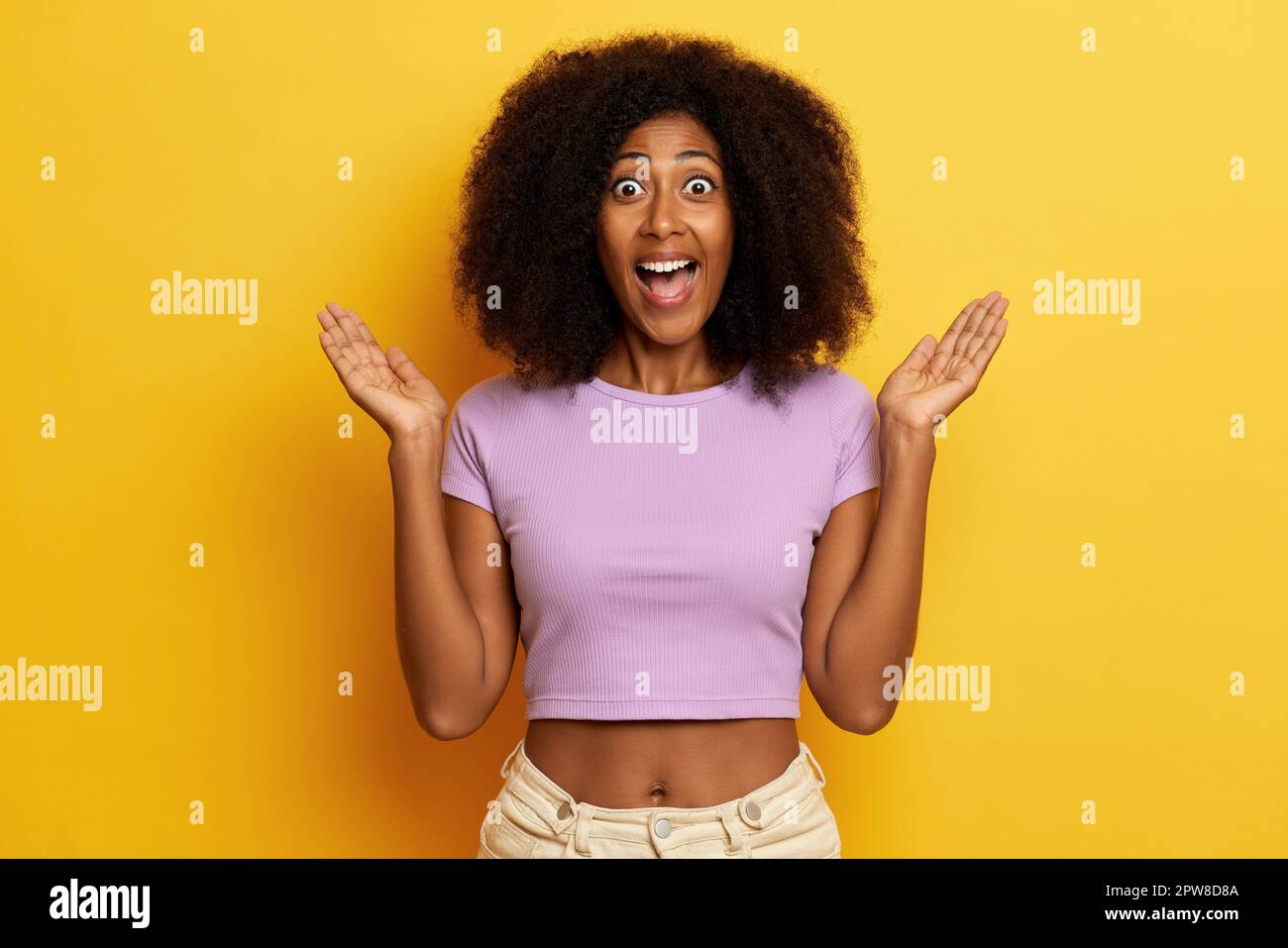 Surprised curly haired woman smiling toothily with opened wide mouth ...