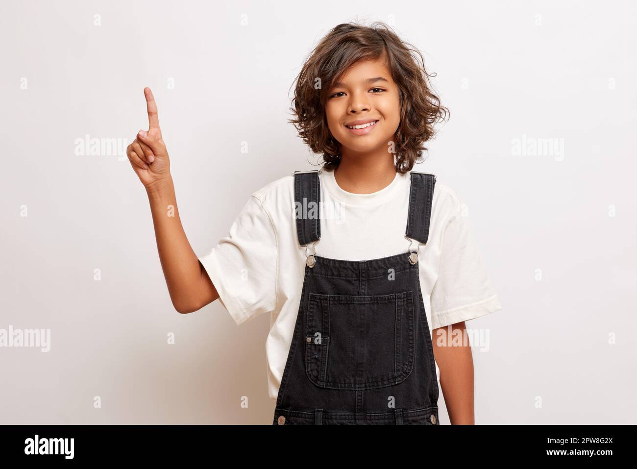 Cute brunette curly haired young guy points index finger at empty space ...