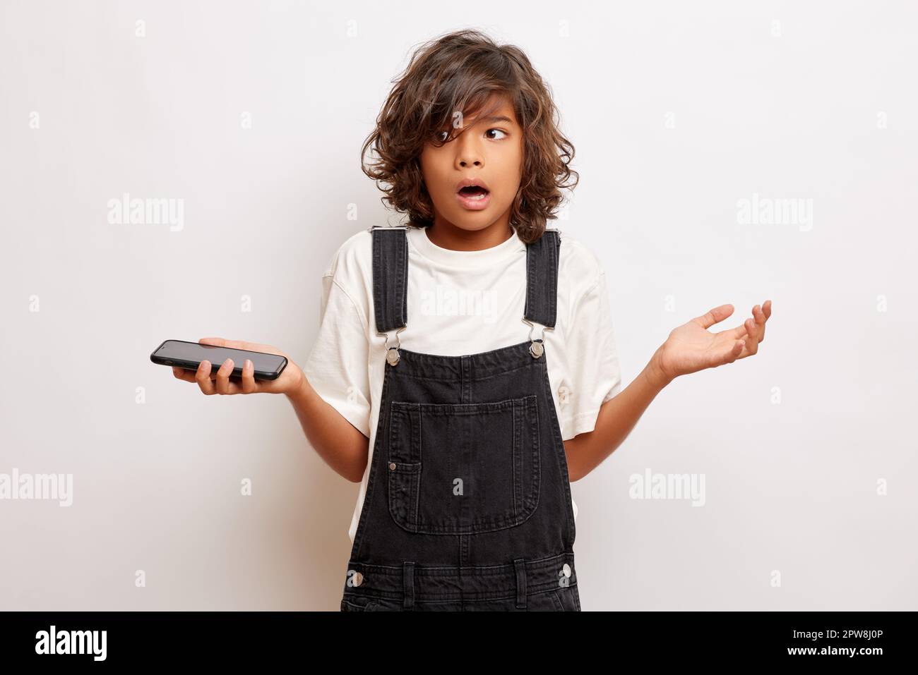 Portrait of confused brunette young guy, holds mobile phone, hesitates ...