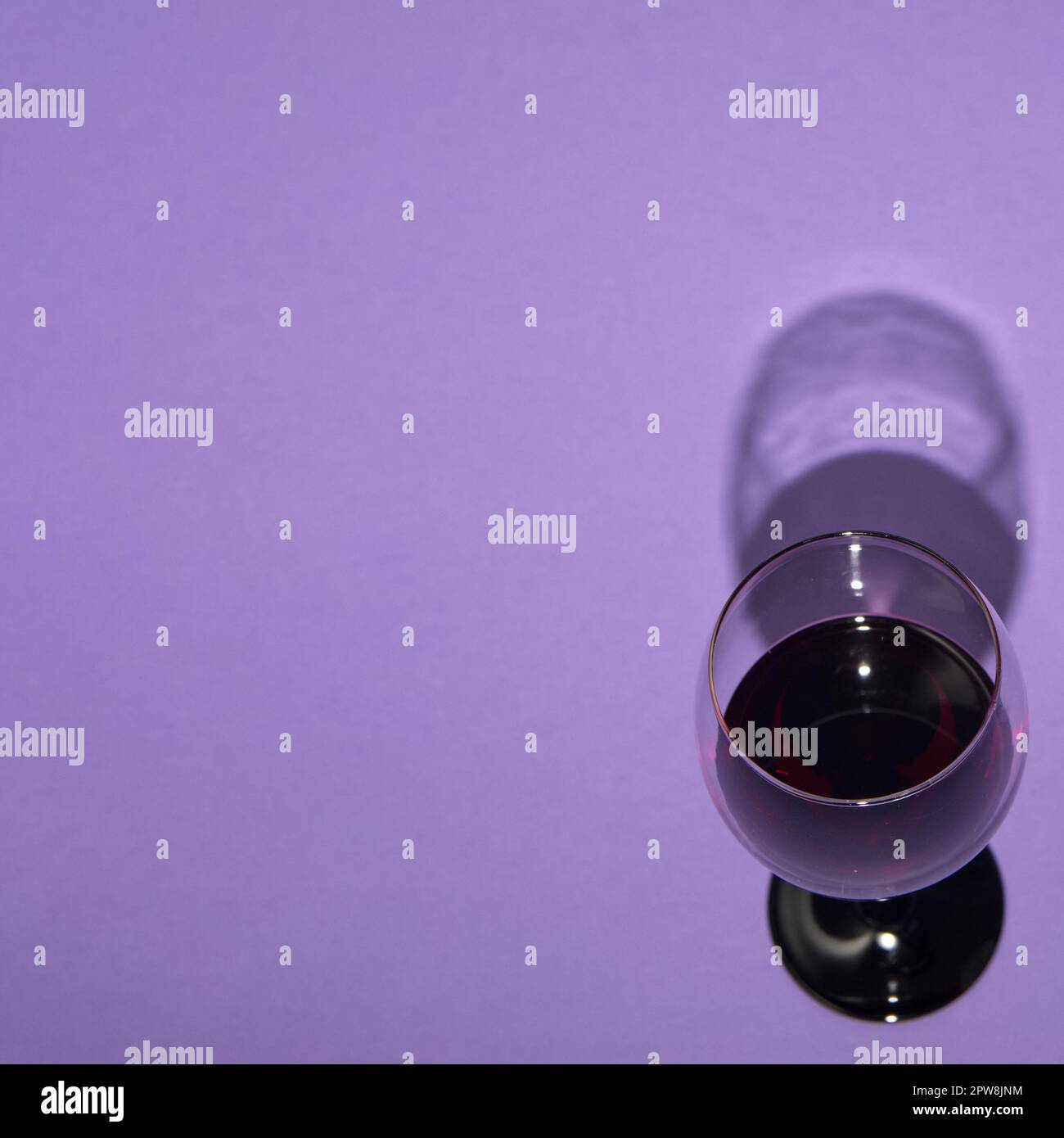 A glass of red wine that casts a shadow on a purple background. Minimal ...