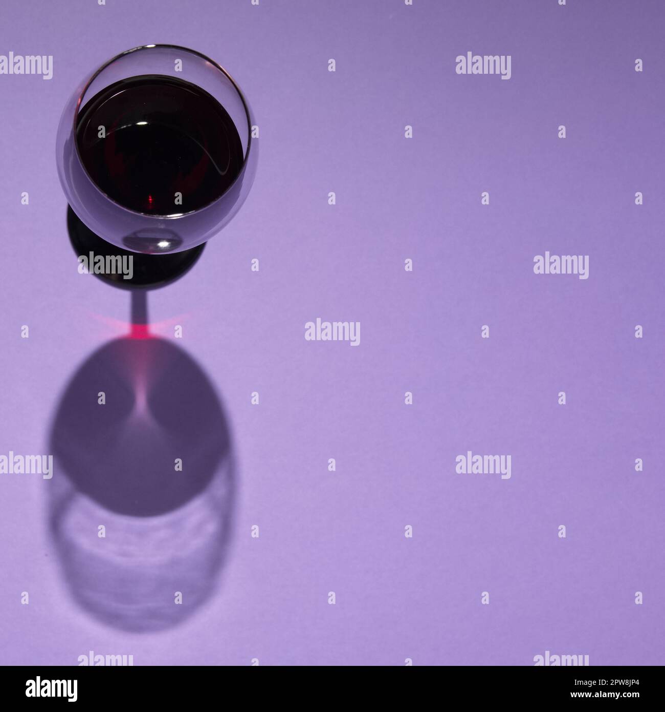 A glass of red wine that casts a shadow and reflects on a purple ...