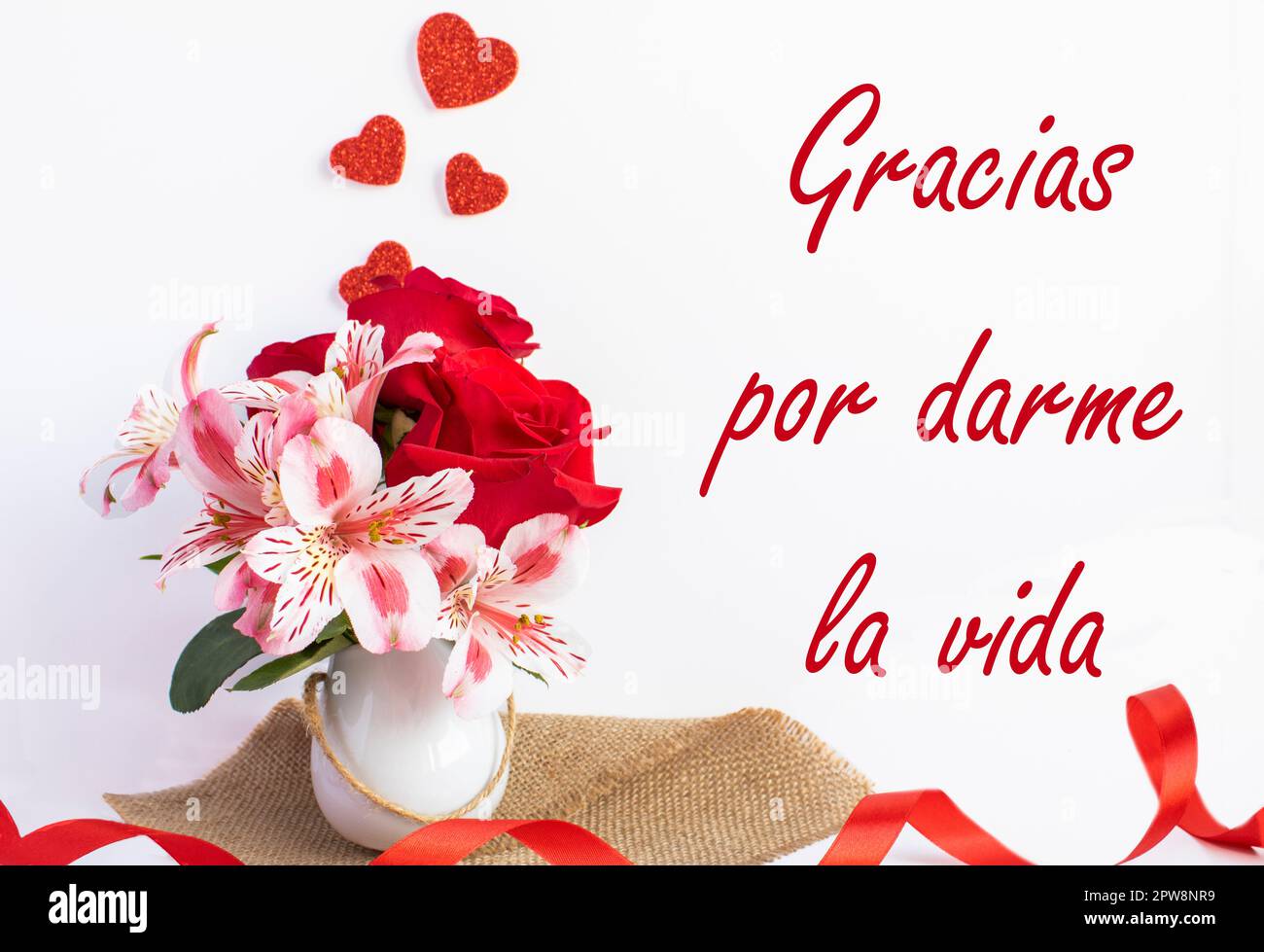 Small white vase with red roses and pink flowers on jute with a red ...