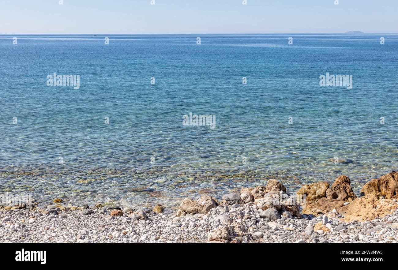 Rocky empty beach transparent calm sea water clear blue sky background ...