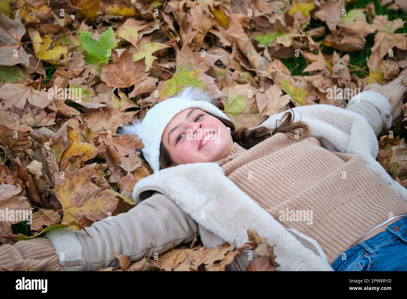 Preteen girl lying down on the ground covered in fallen leaves during ...