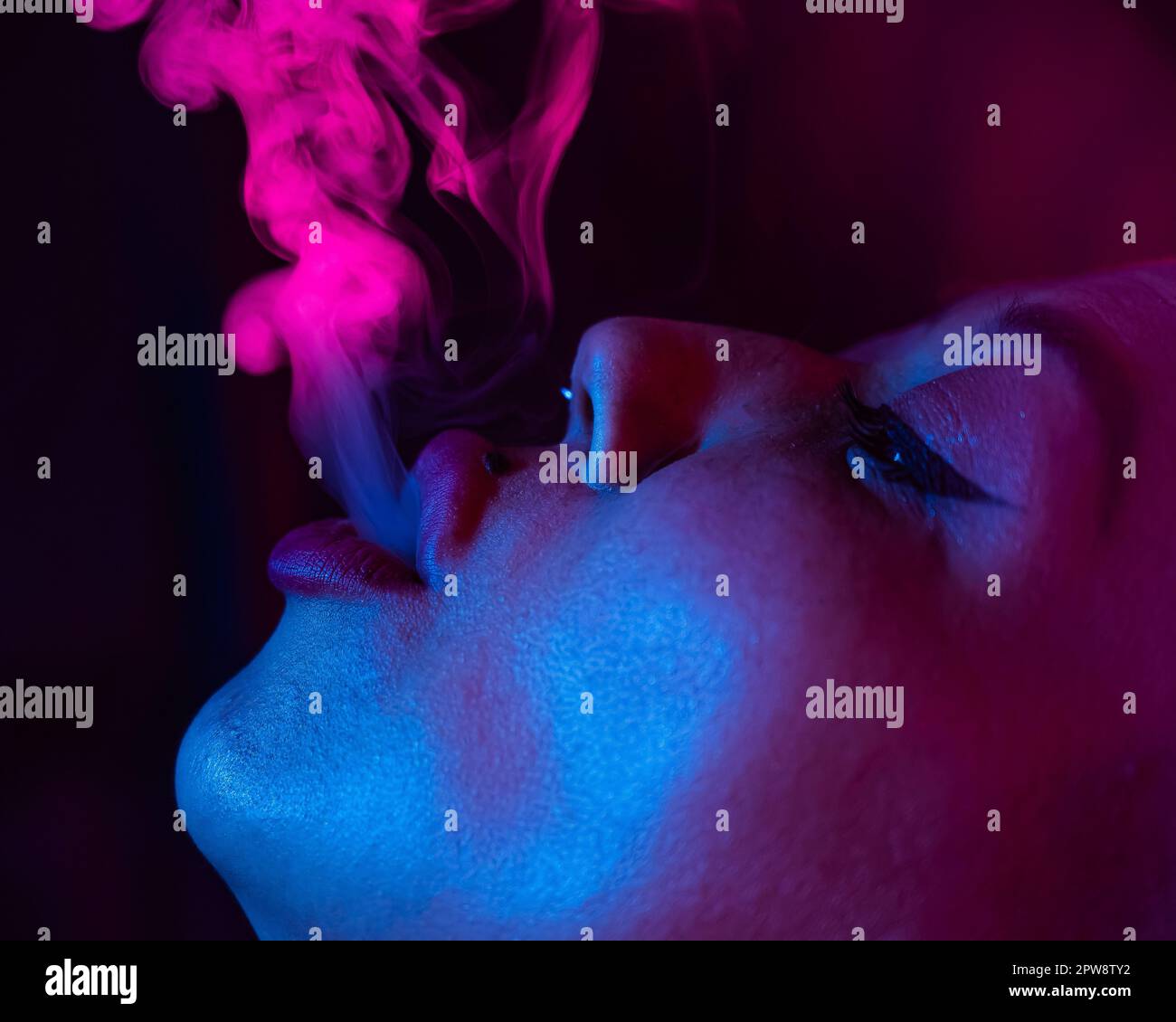 Close up portrait of asian woman with short hair smoking in neon light ...