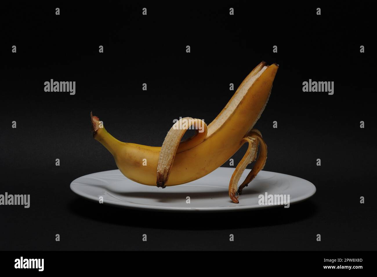 half-peeled banana standing in the air on a porcelain plate on a black ...
