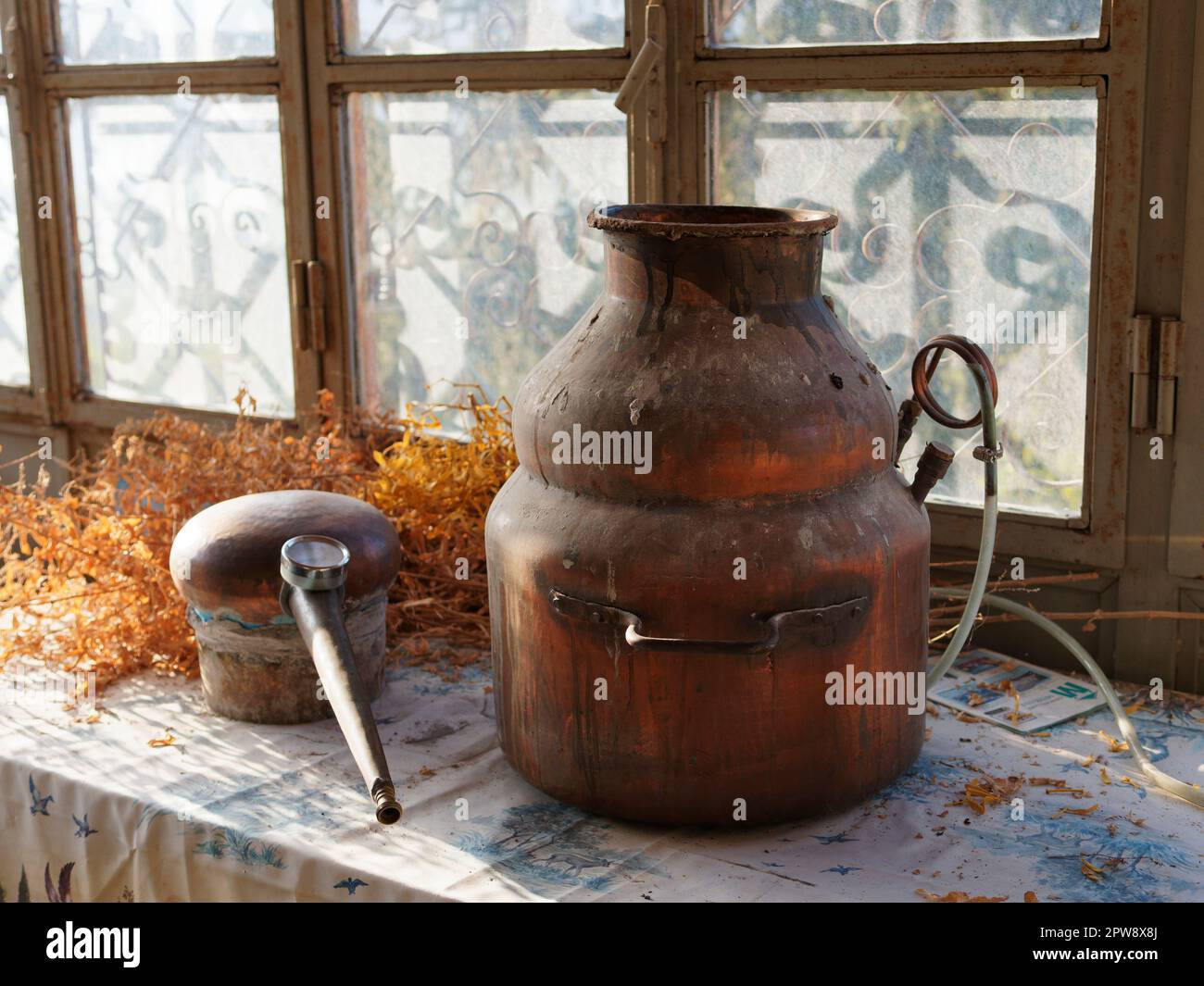 Old rustic Distillation Equipment on a table in front of a window with ...