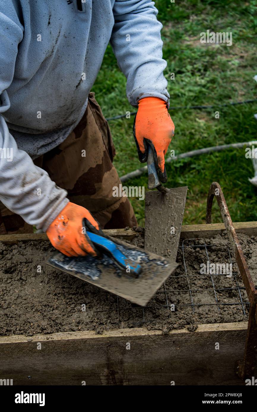 Bricklayer spreading concrete with a trowel and level to build a wall ...