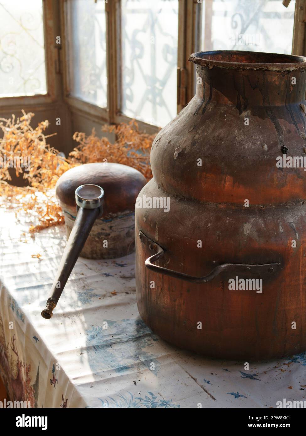 Old rustic Distillation Equipment on a table in front of a window with ...