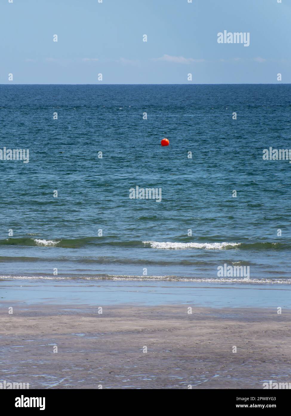 Blue sea water and a sandy beach under a blue sky. Orange buoy on the ...