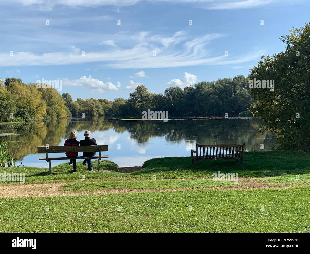 Couple sat on park bench overlooking one of the lakes at Emberton ...