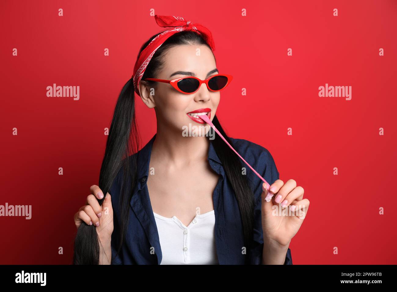 Fashionable young woman in pin up outfit chewing bubblegum on red ...
