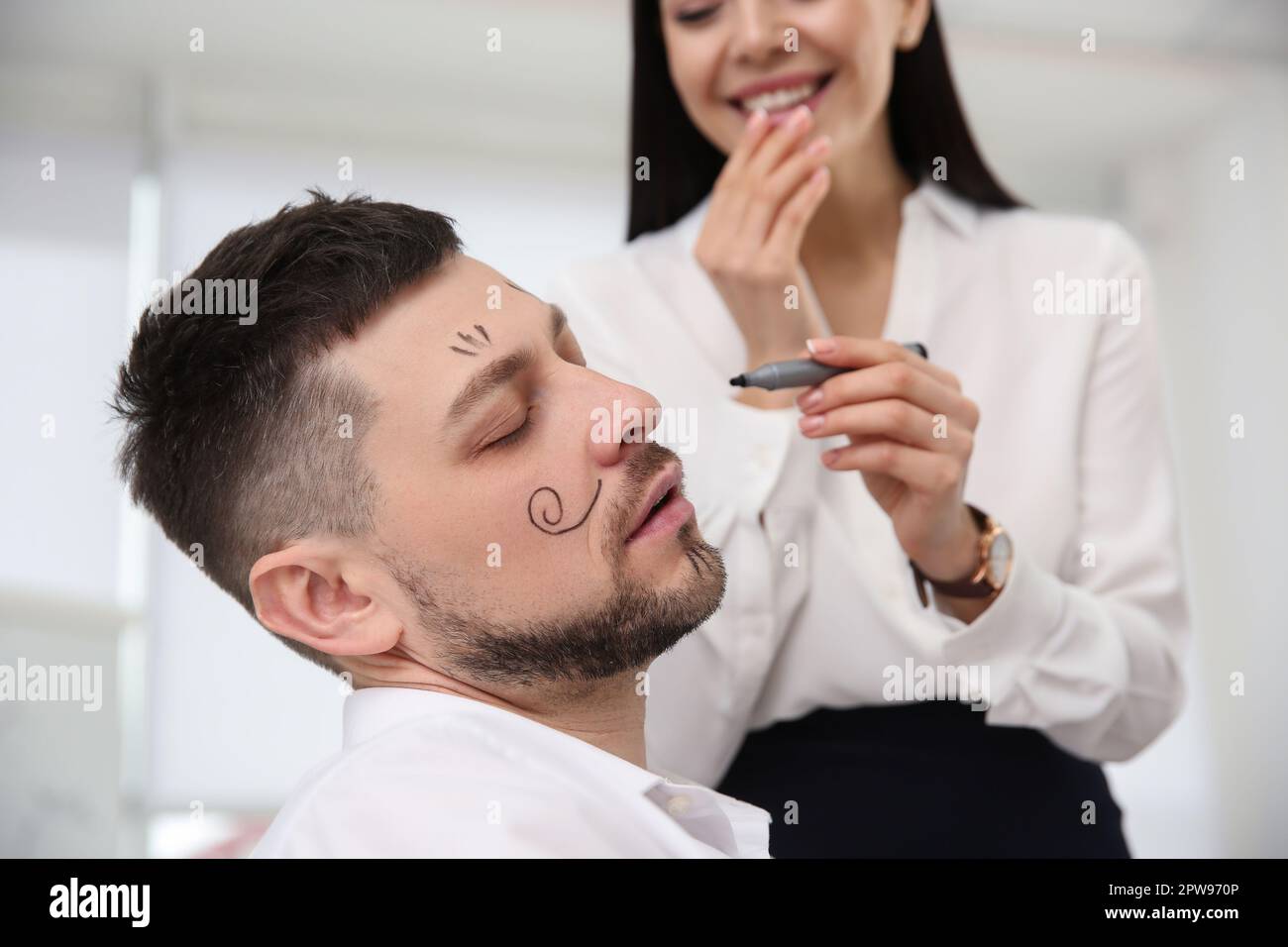 Young woman drawing on colleague's face while he sleeping in office ...