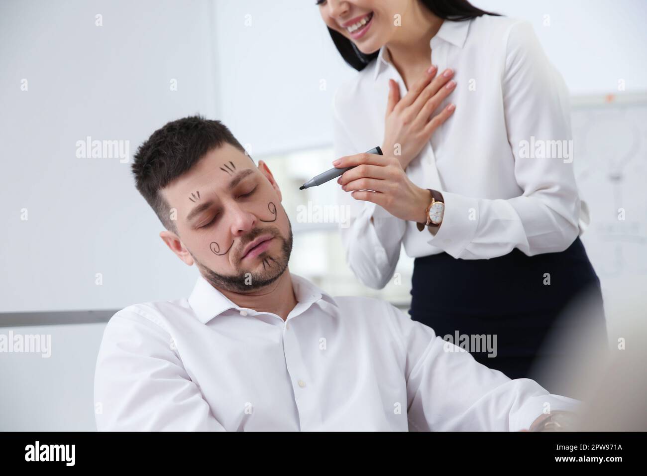 Young woman drawing on colleague's face while he sleeping in office ...