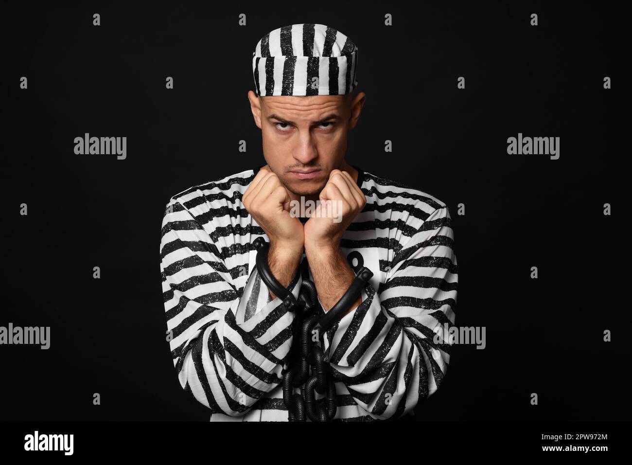 Prisoner in striped uniform with chained hands on black background ...