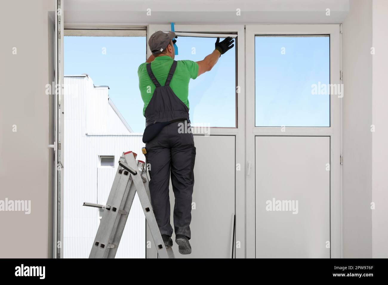 Worker on folding ladder installing window indoors, back view Stock ...