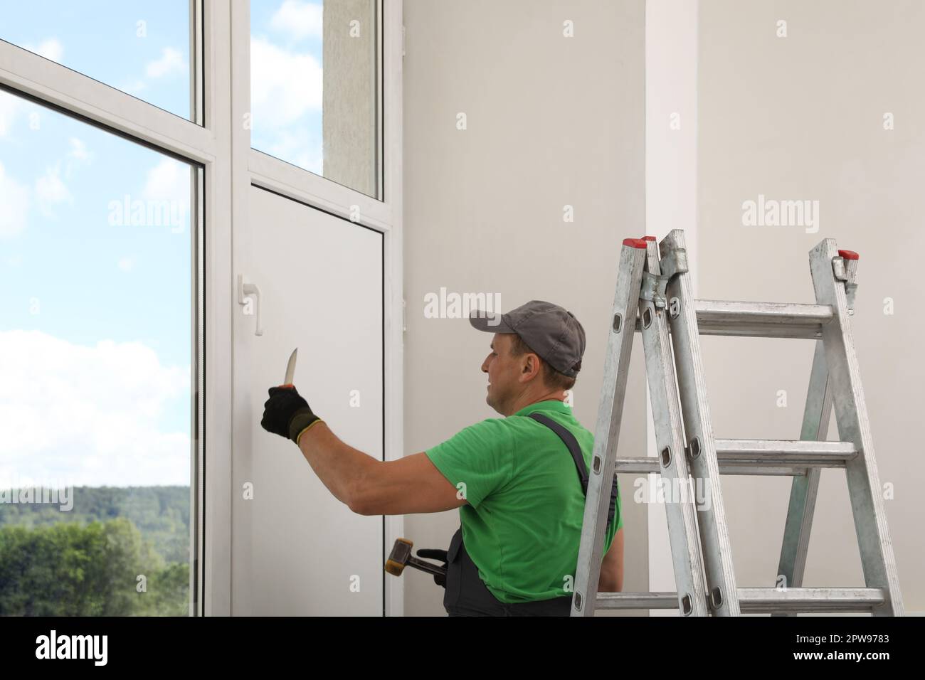 Worker holding knife and hammer indoors. Window installation Stock ...