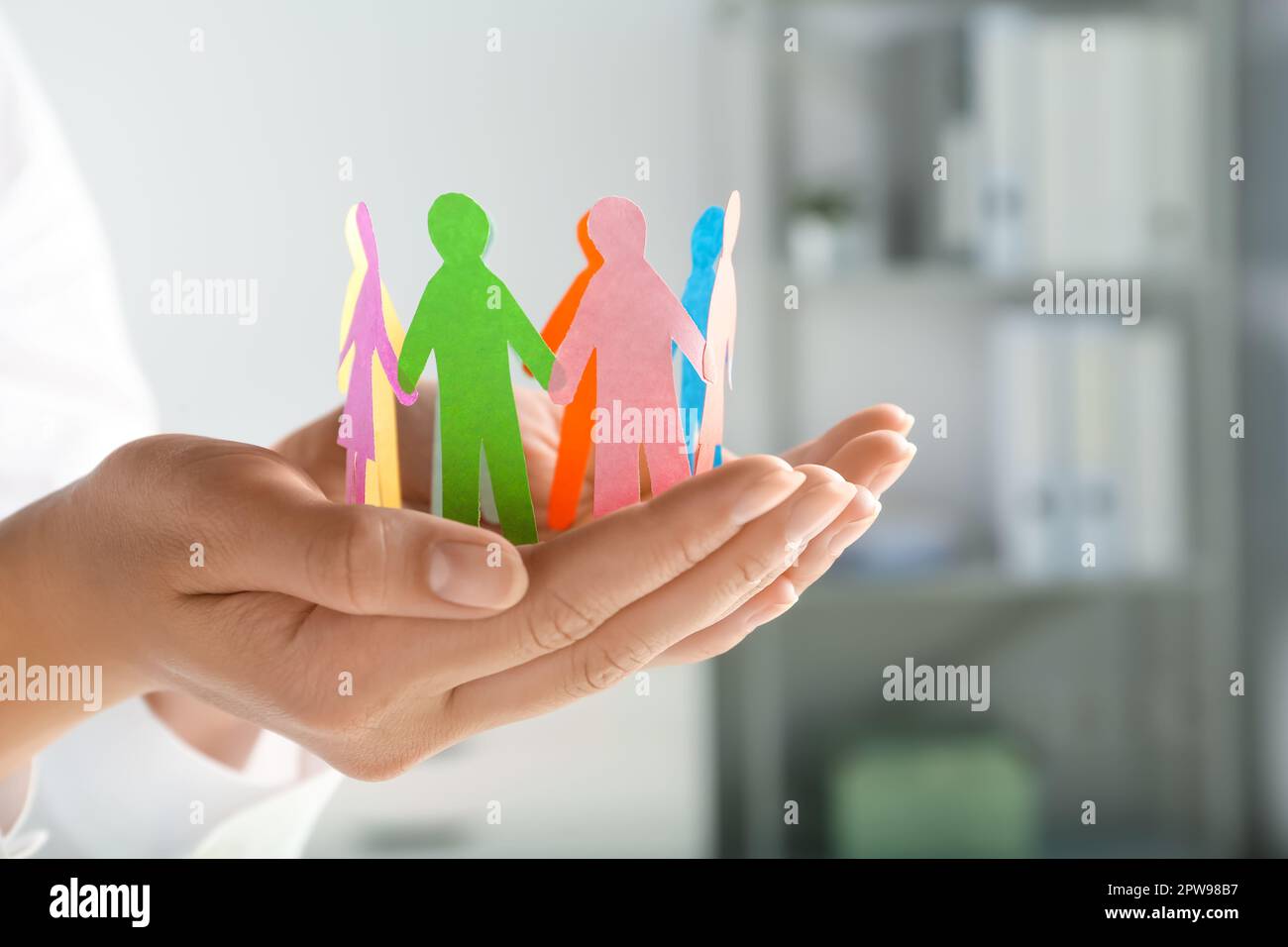 Woman holding paper human figures on blurred background, closeup ...