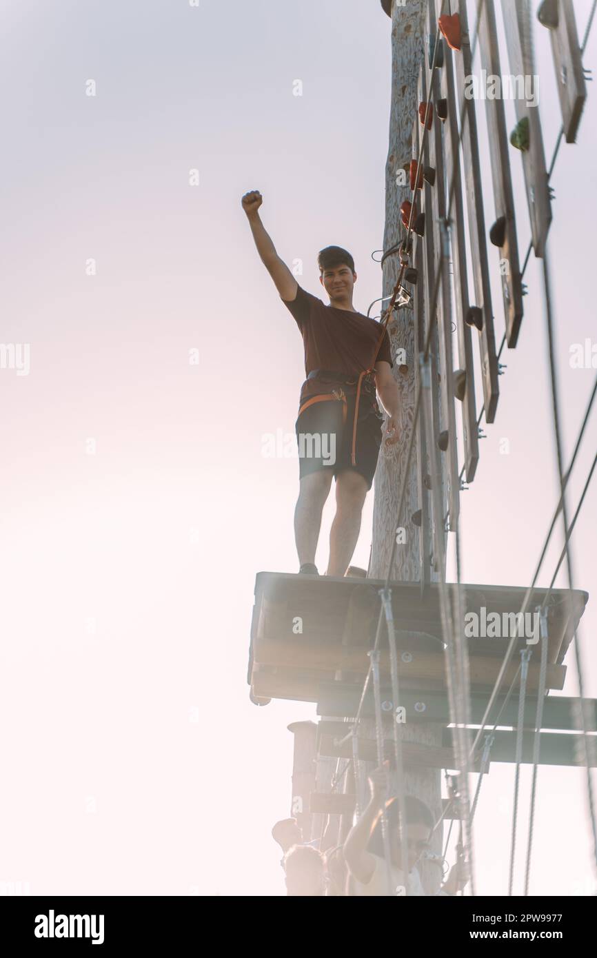 Strong man standing on the top with his hand up at the adventure park ...