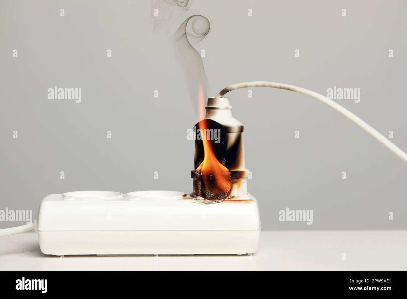 Inflamed plug in power strip on white table against grey wall ...