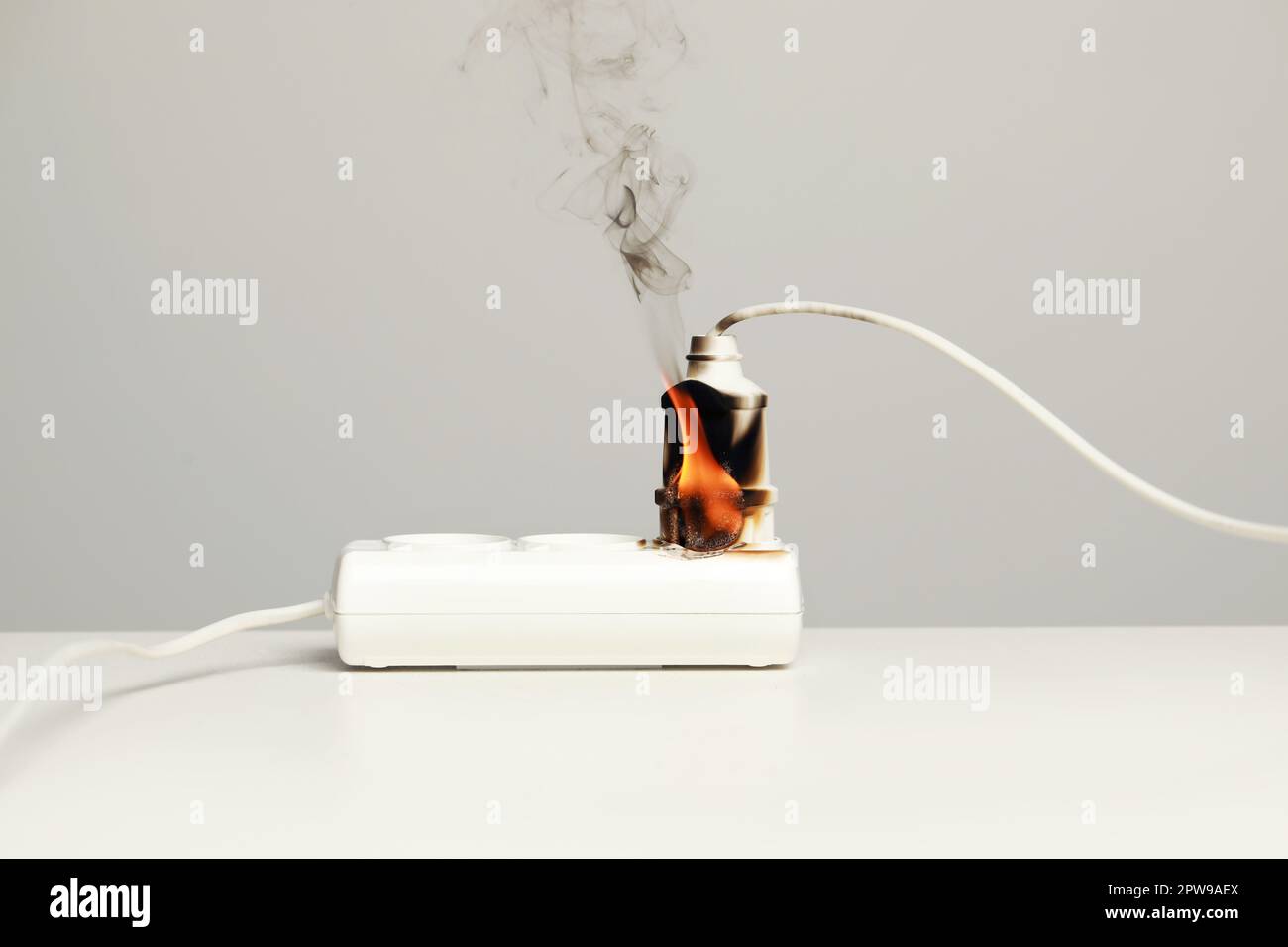 Inflamed plug in power strip on white table against grey wall ...