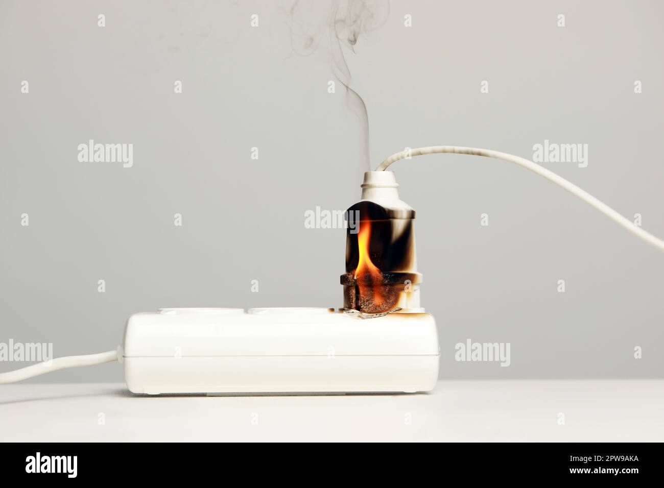Inflamed plug in power strip on white table against grey wall ...