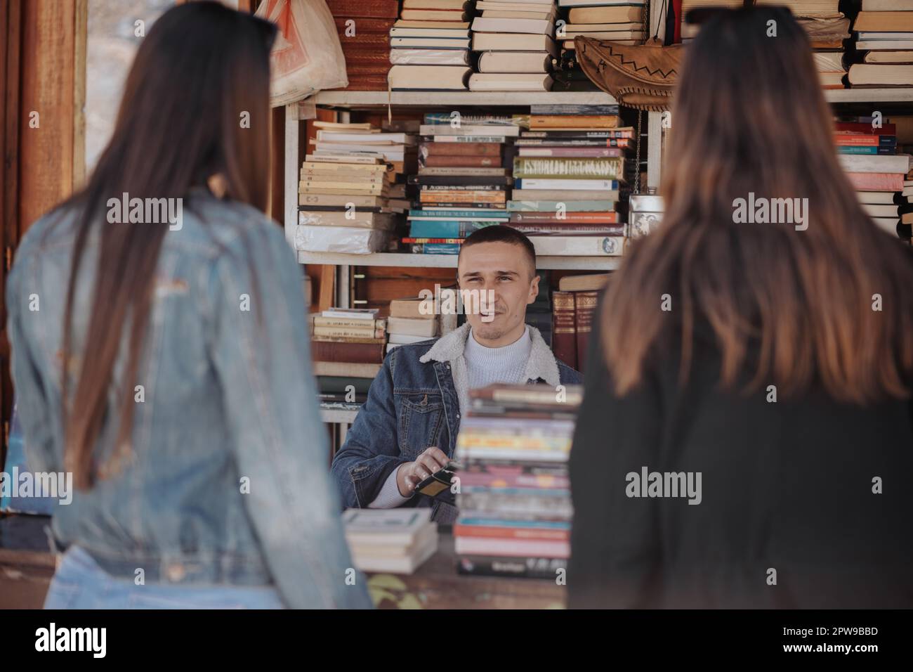 Two girls talking about book with the book seller while standing at the ...