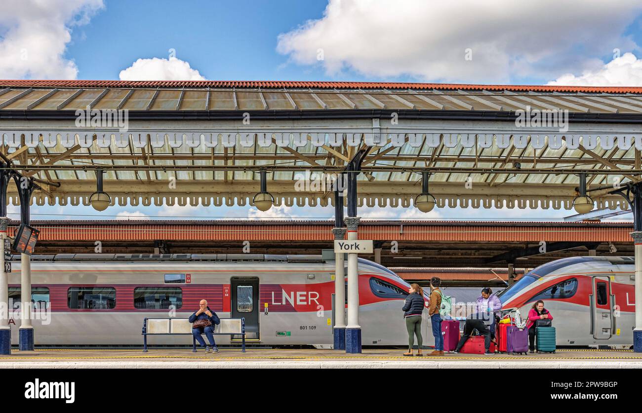 Passengers wait on a railway station platform for a train. Two ...