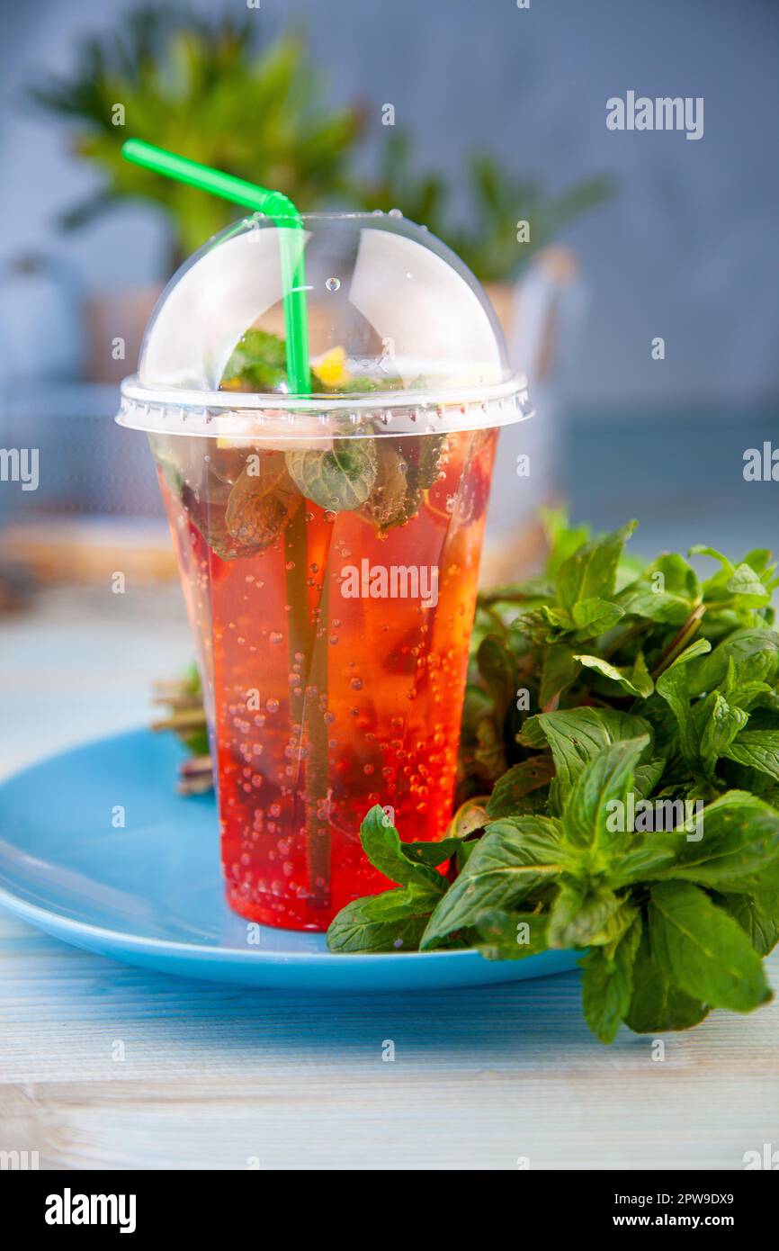 Summer mint strawberry refreshing cocktail mojito with ice in plastic glass with straw ...